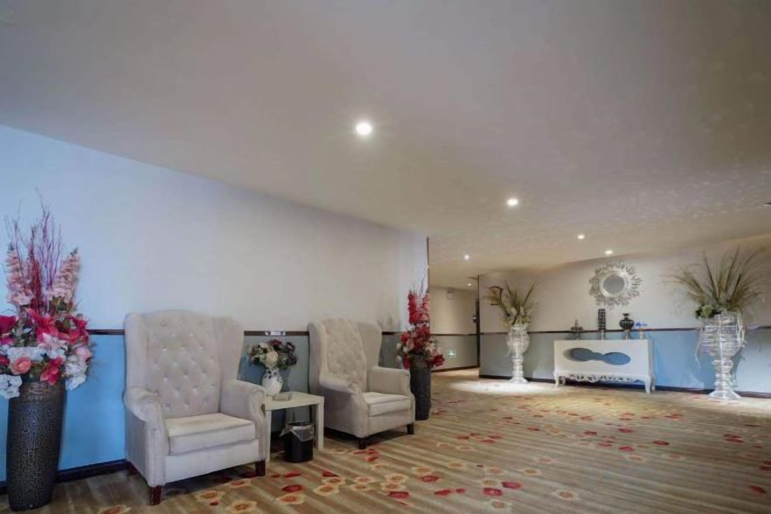 Um saguão de hotel com duas poltronas, uma mesa pequena e um aparador decorativo.