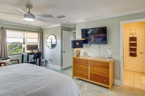Um quarto com uma cama, uma escrivaninha, uma televisão, uma cômoda e uma porta.