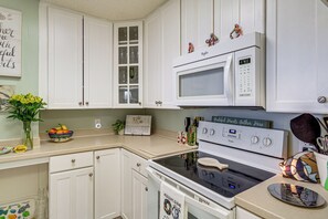 Uma cozinha com armários brancos, micro-ondas, fogão por indução e diversos utensílios.