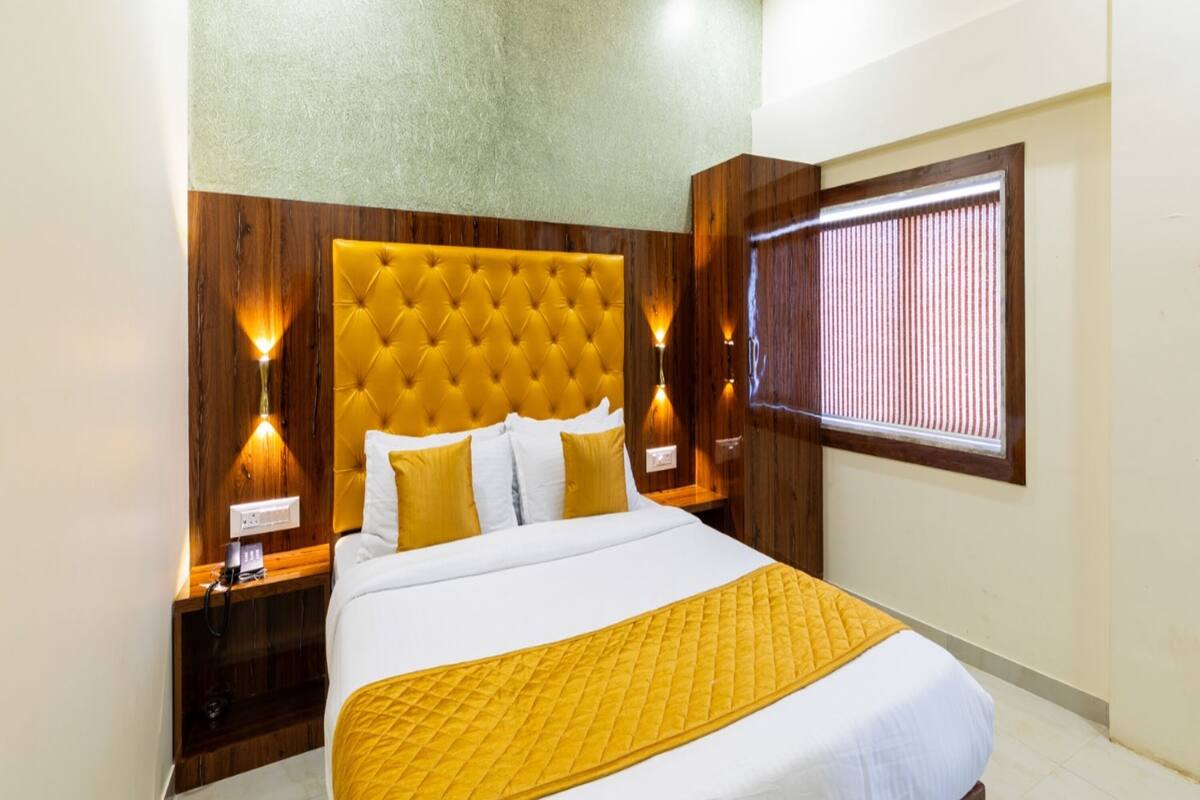 Quarto de hotel com uma cama grande, cabeceira de madeira, abajures e uma janela com persianas.