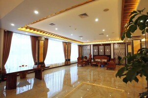 Um hall amplo com piso lustroso, balcão de recepção, área de estar e grandes janelas.