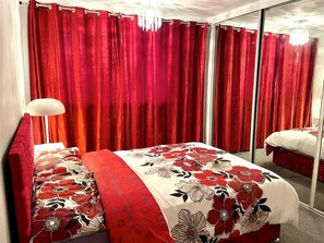 Quarto com cama, espelho e cortinas vermelhas.