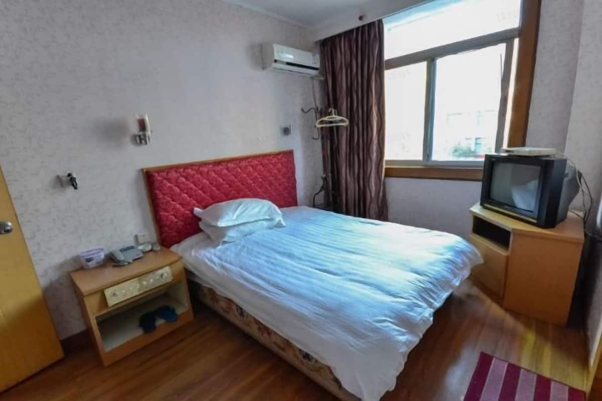 Quarto de hotel com cama, televisão, mesa de cabeceira, guarda-roupa e janela com cortinas.