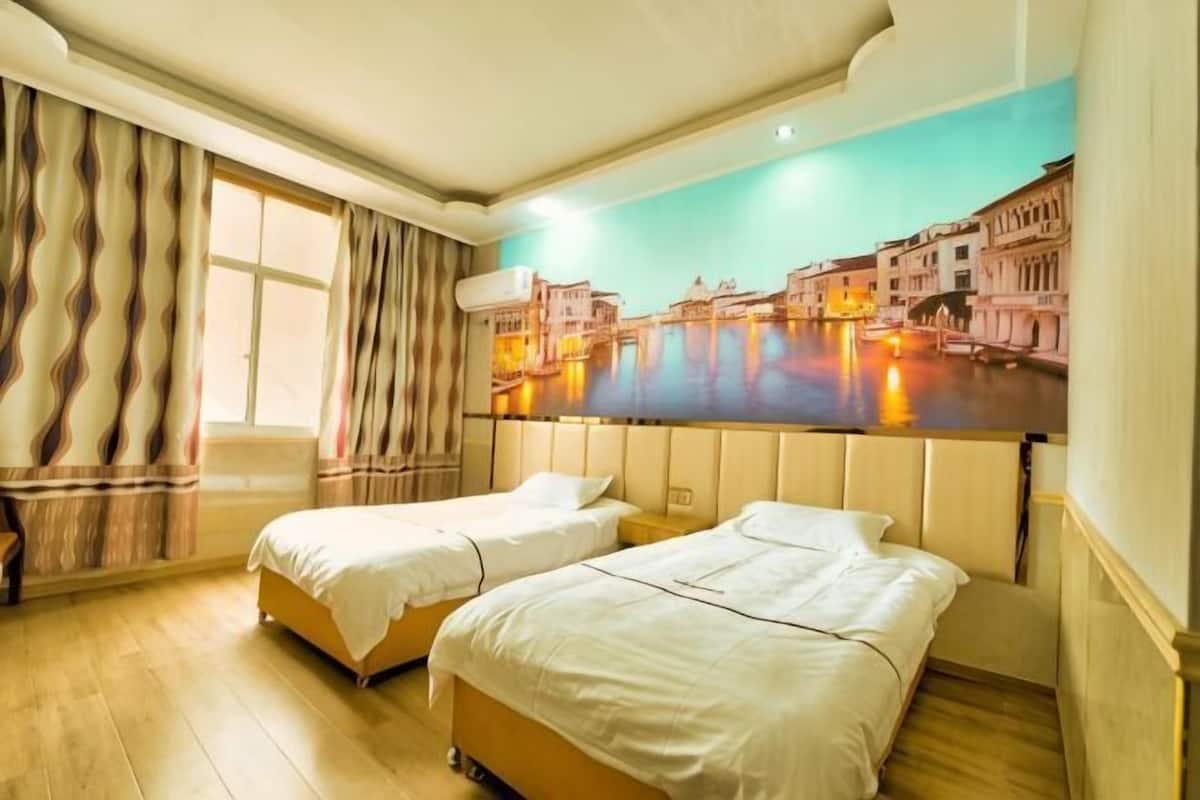 Quarto de hotel com duas camas, uma janela grande com cortinas e um mural com uma cena de canal.