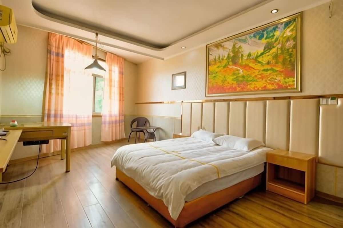 Quarto com cama, escrivaninha, cadeira, quadro e janela com cortinas.