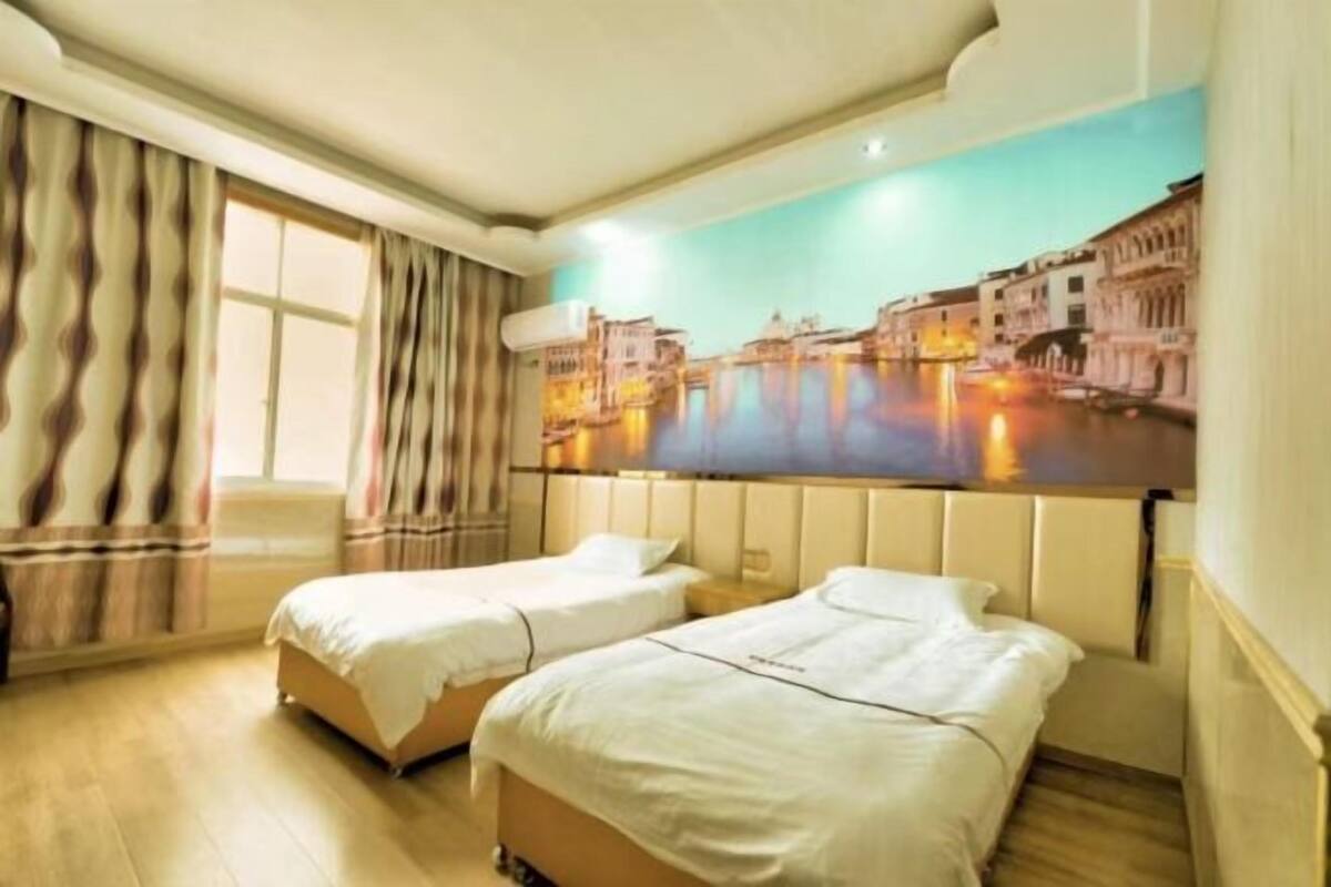 Quarto de hotel com duas camas, uma janela grande com cortinas e um mural retratando uma paisagem urbana.