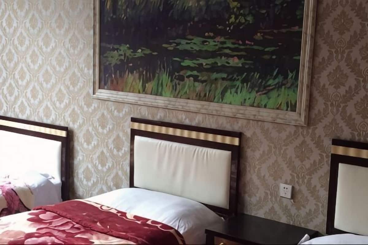Quarto de hotel com duas camas, um quadro de um lago, papel de parede estampado e uma mesa de cabeceira.