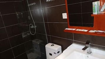 Casa de banho com cabine de duche em vidro, uma pia branca com torneira moderna e um armário com produtos de higiene pessoal.