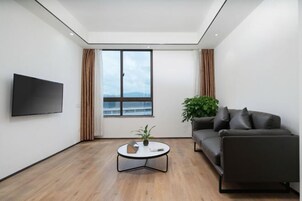 Uma sala de estar moderna com televisão de tela plana, mesa de centro redonda, sofá, uma janela grande com cortinas e um vaso de planta.