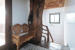 Um banco de madeira, um tronco de árvore grande e uma janela num quarto.