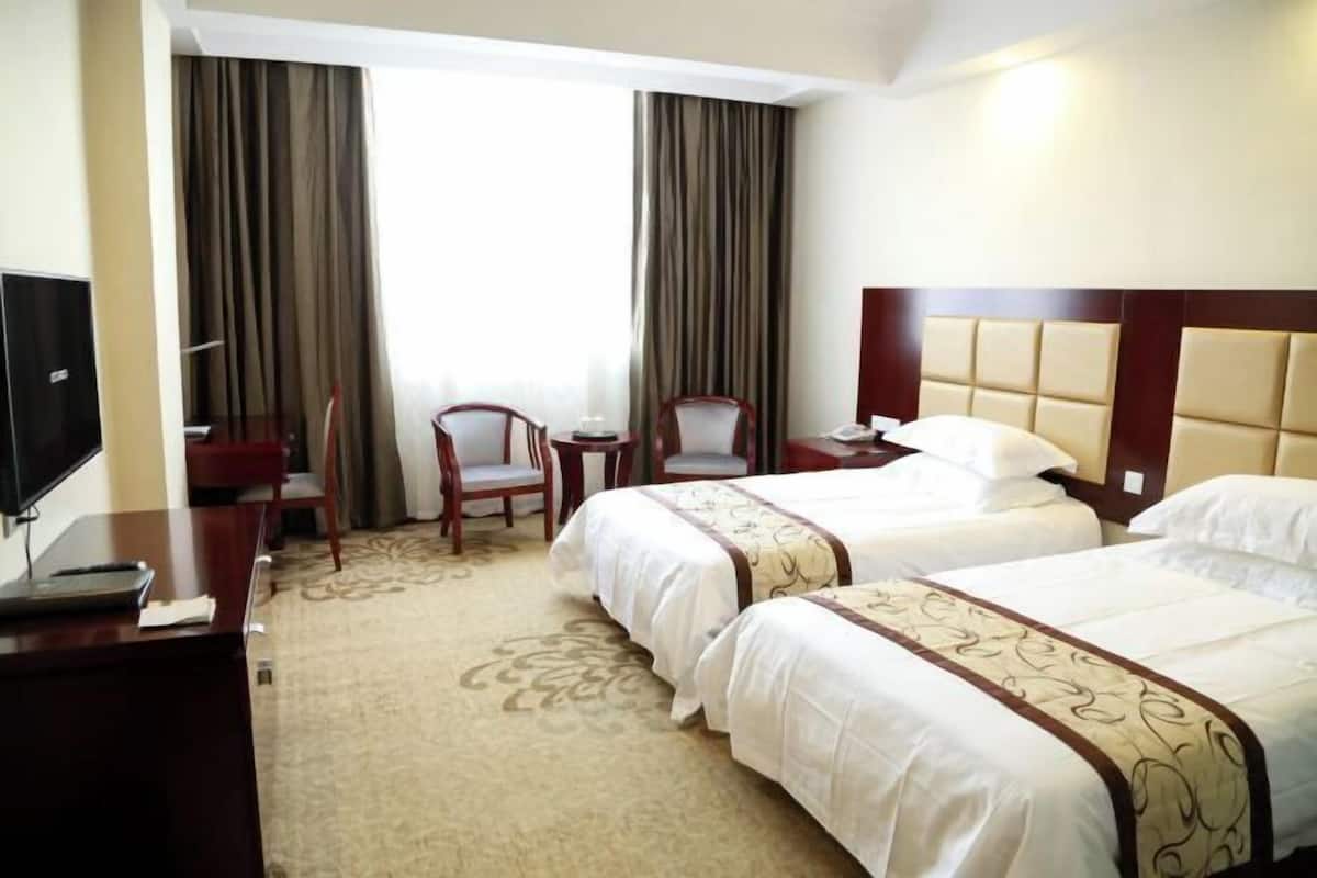 Quarto de hotel com duas camas, uma mesa, uma cadeira, uma televisão e cortinas.