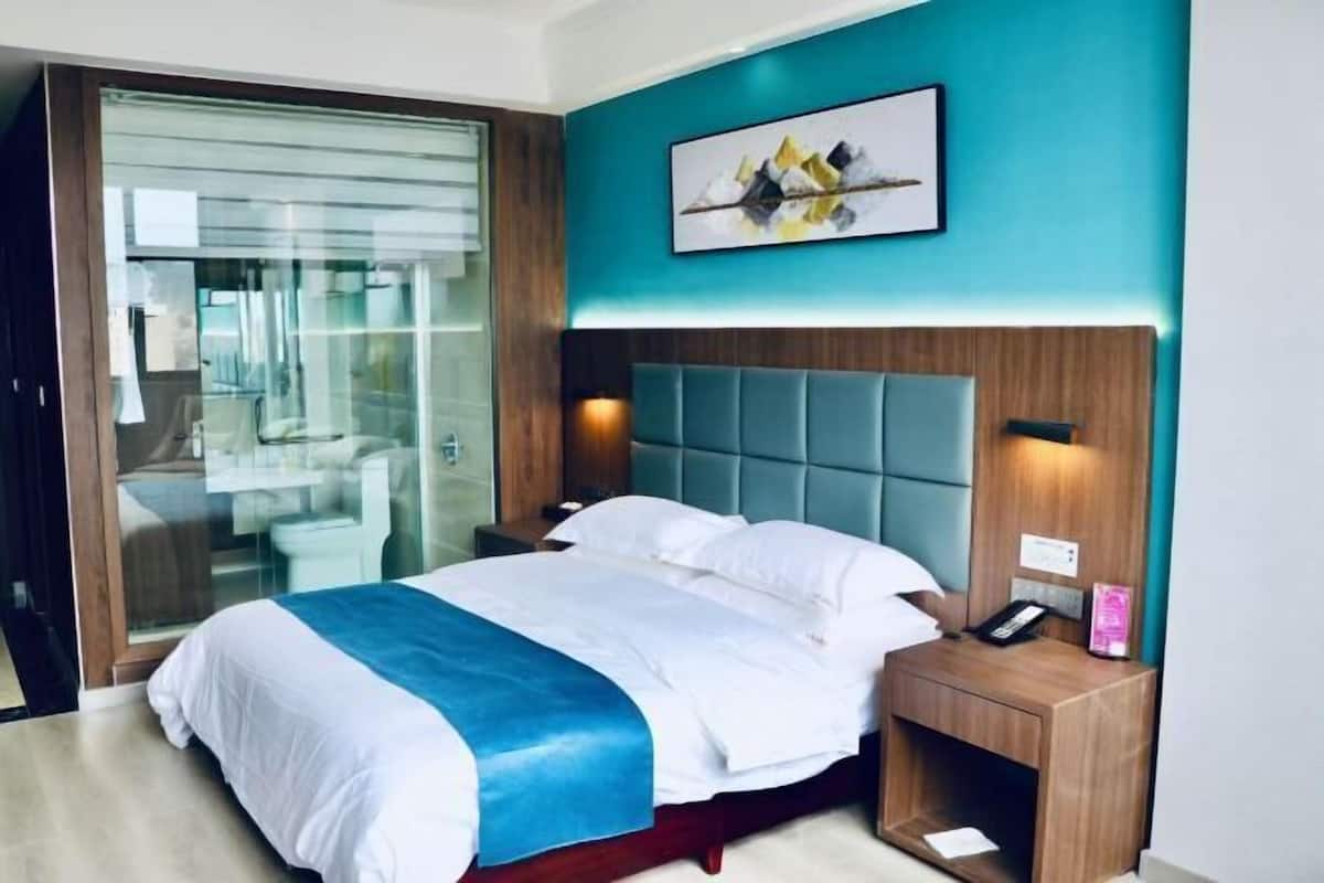 Quarto de hotel moderno com uma cama grande, porta de vidro para um banheiro e uma parede de destaque verde-água.