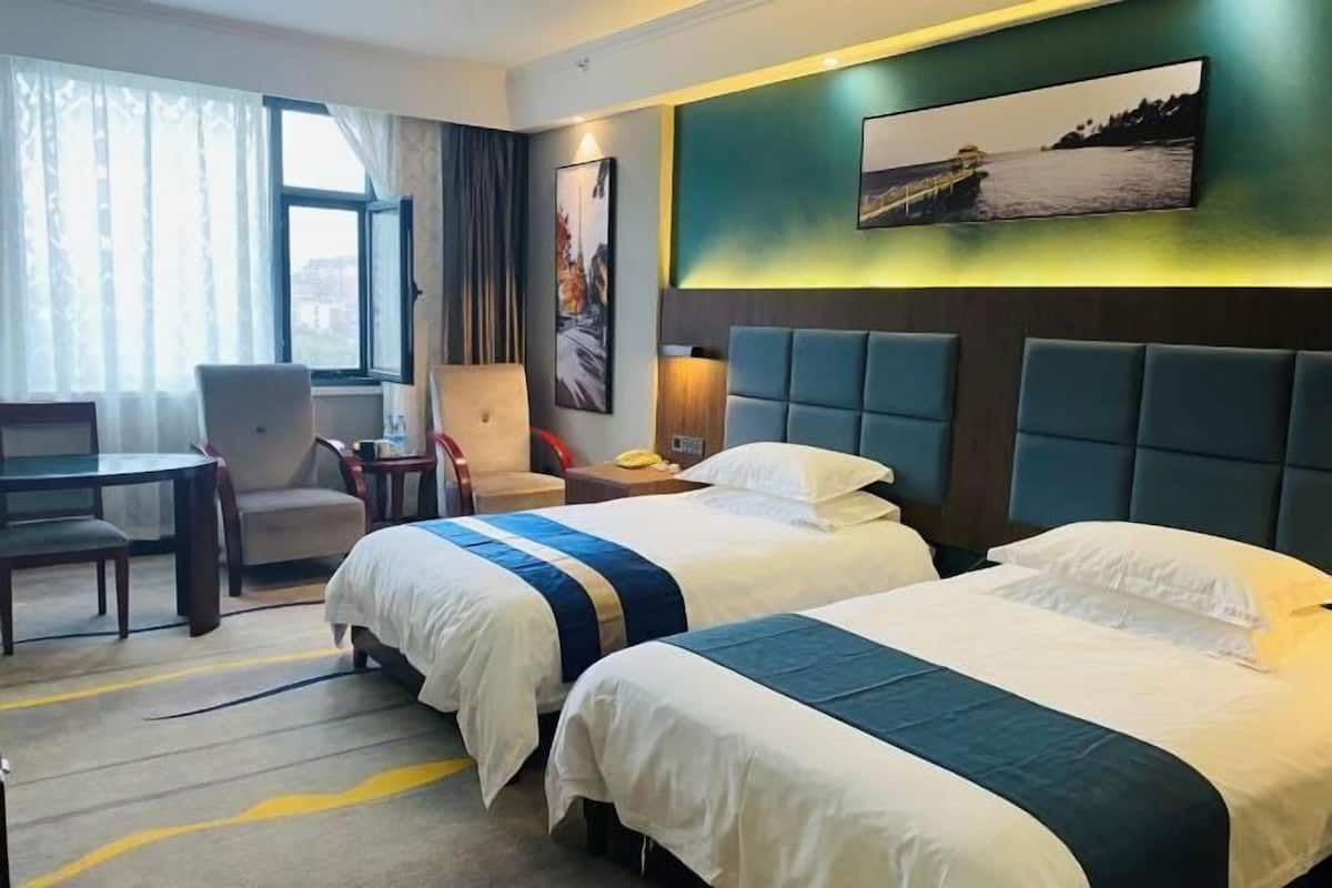 Quarto de hotel com duas camas, uma escrivaninha, uma cadeira, uma janela com cortinas e um quadro na parede.