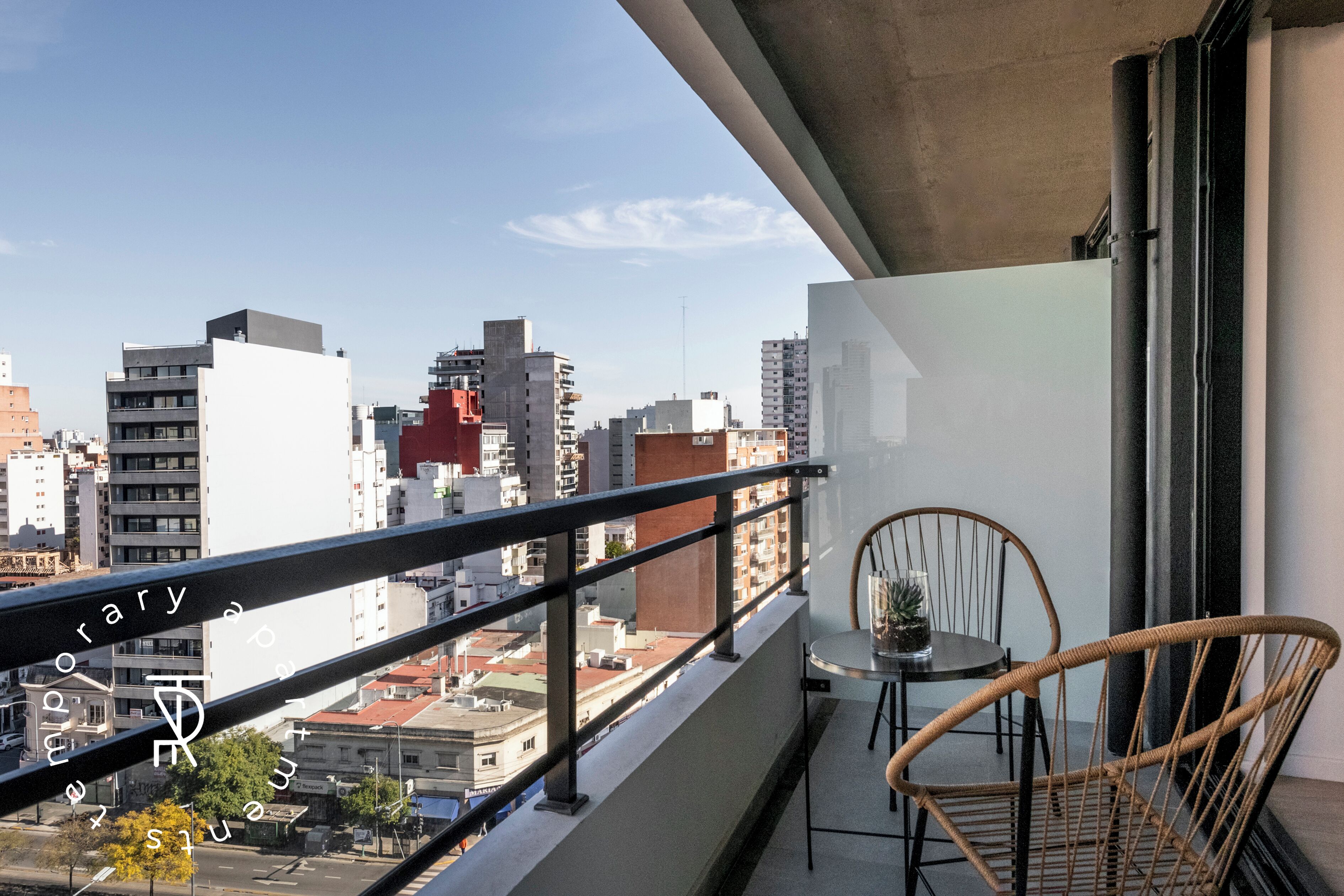 Uma varanda com vista para a cidade, uma mesa pequena com uma cadeira e um vaso de planta.