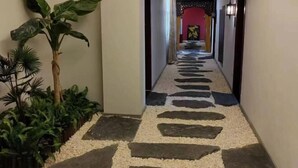 Um corredor com piso em padrão de pedras, uma planta grande à esquerda e uma porta no final.