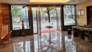Um hall de hotel com piso reluzente, balcão de recepção e vista para a rua.