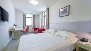 Quarto de hotel com uma cama grande, uma mesa com cadeira, televisão na parede e um quadro emoldurado.