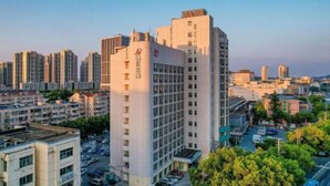 Um edifício alto com design arquitetônico moderno, cercado por outros edifícios residenciais e um estacionamento.