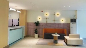 Uma área de receção moderna, com balcão, zona de estar e iluminação decorativa na parede.