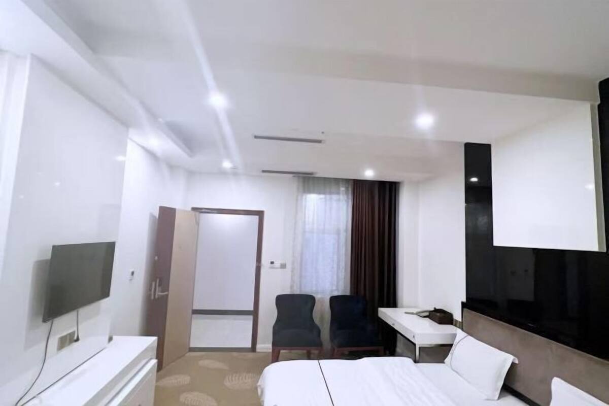 Quarto de hotel com cama, escrivaninha, cadeira, televisão e porta.