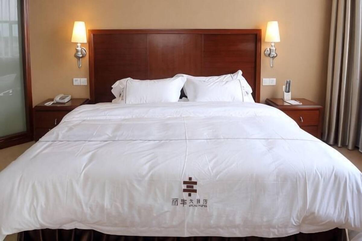 Quarto de hotel com uma cama grande, duas luminárias de cabeceira, mesa de cabeceira com telefone e luminária na parede.