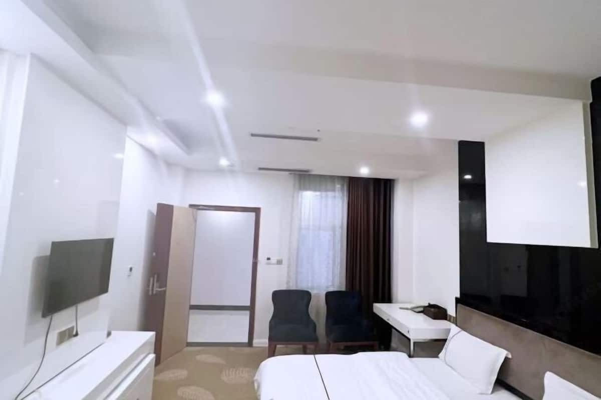 Quarto de hotel com uma cama, televisão, escrivaninha, duas cadeiras e uma porta.