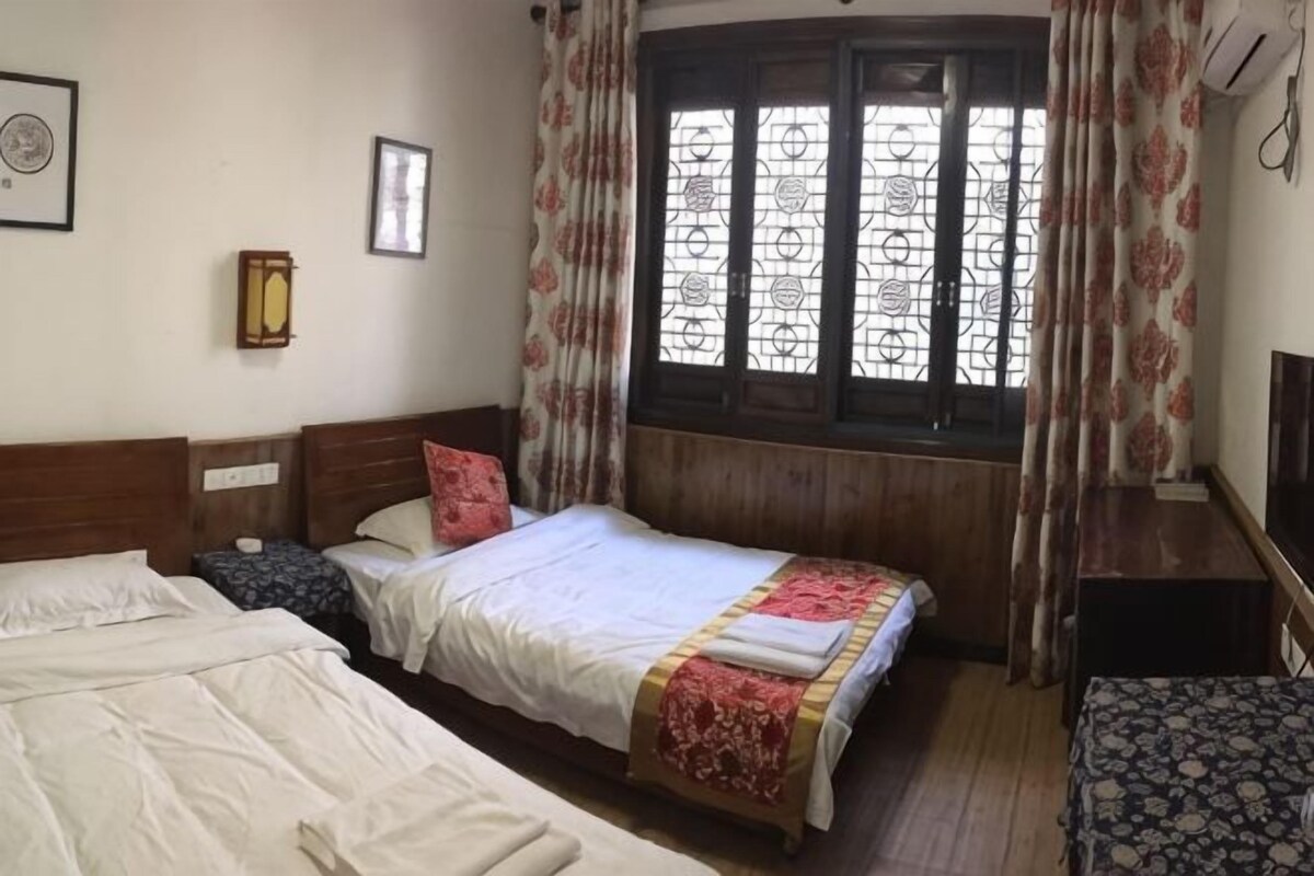 Quarto com duas camas, cabeceira de madeira, janela com cortinas e televisão na parede.