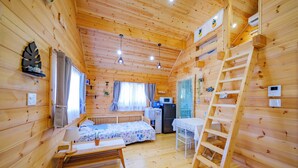 Quarto de cabana de madeira com cama, escrivaninha, escada, mesa pequena, radiador e janela com cortinas.