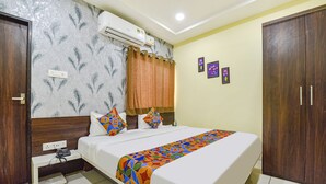 Quarto de hotel com cama, guarda-roupa, mesa de cabeceira, ar condicionado e tomada na parede.