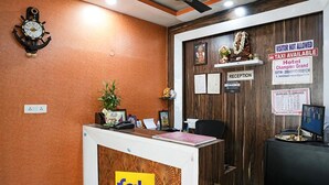 Bancada de recepção de hotel com parede de madeira, um relógio e uma placa indicando a área de recepção.