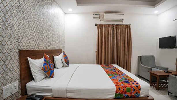 Quarto de hotel com uma cama, televisão, poltrona e ar condicionado.