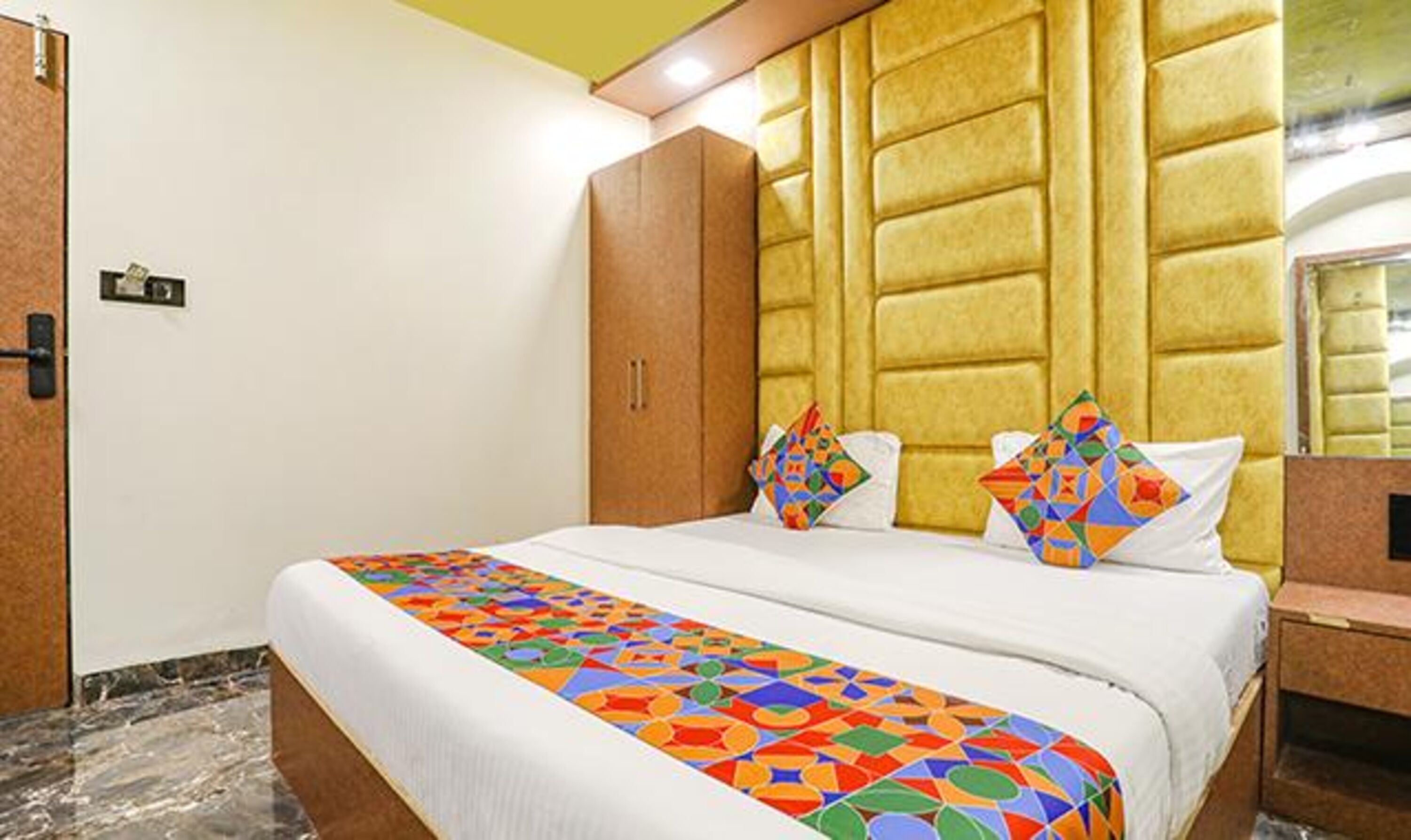 Quarto de hotel com cama, mesa de cabeceira, guarda-roupa e cabeceira com padrão geométrico.