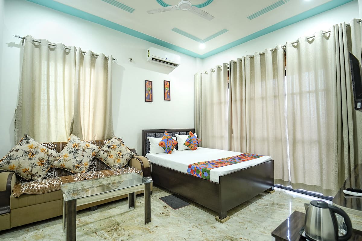Quarto de hotel com cama, sofá, mesa de centro, cortinas, ar condicionado e ventilador de teto.
