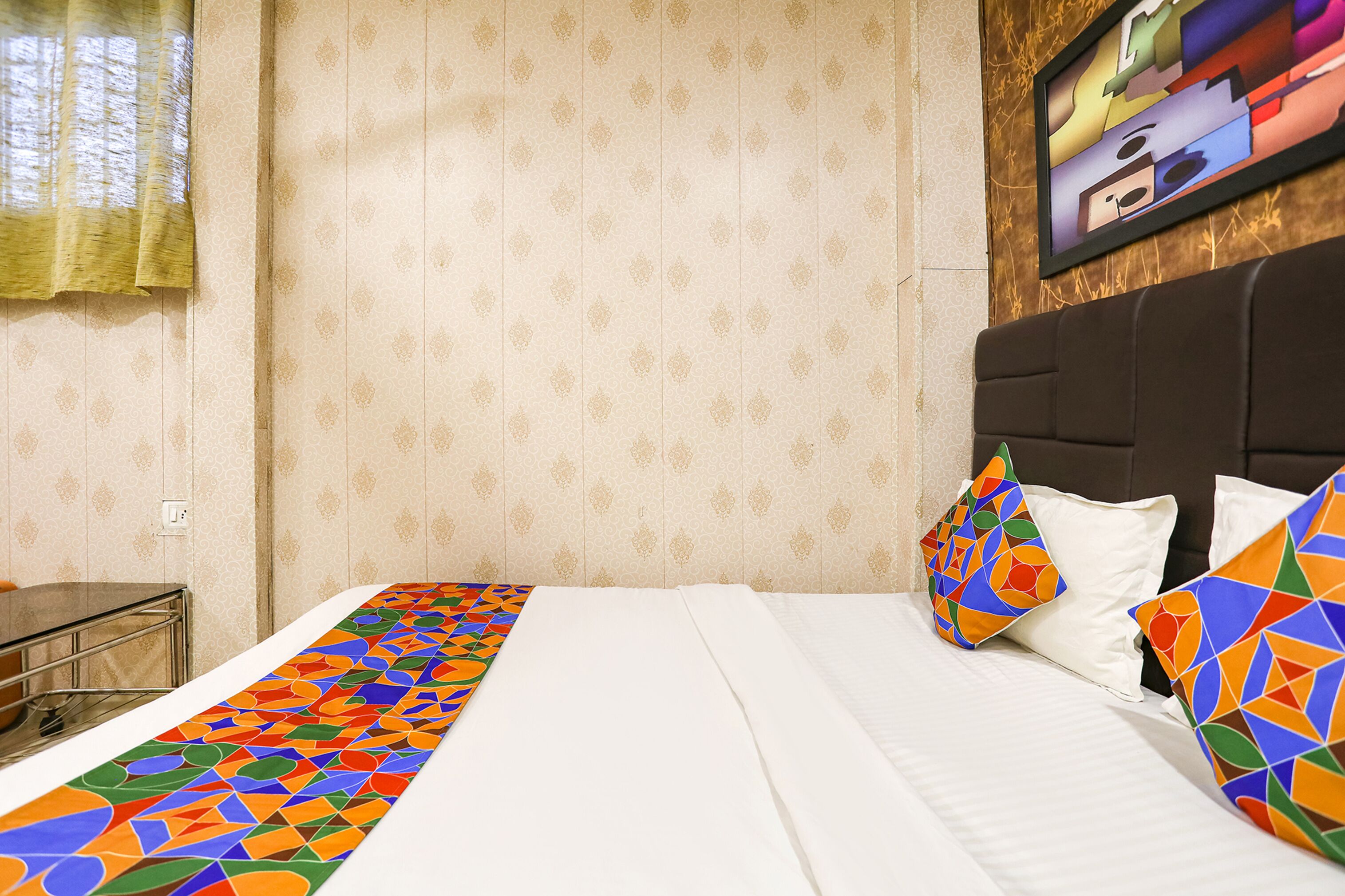 Quarto de hotel com cama, um tapete colorido, cabeceira e um quadro na parede.