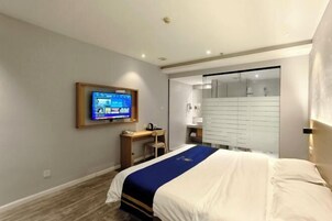 Quarto de hotel com cama, escrivaninha, televisão e guarda-roupa.
