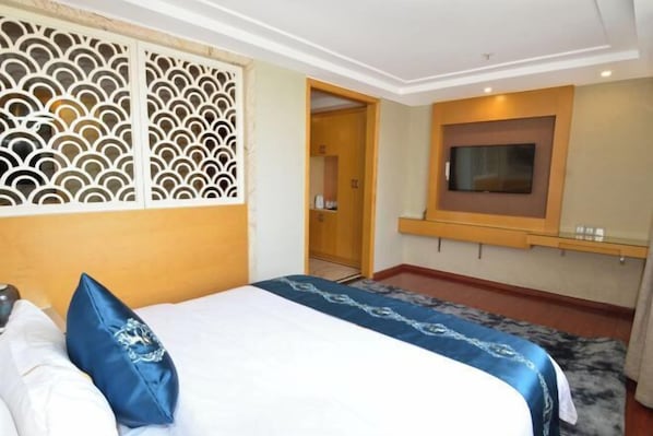 Quarto com cama, TV fixada na parede e porta de madeira que dá para um banheiro.