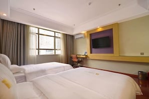 Quarto de hotel com duas camas, uma mesa, uma cadeira, televisão fixada na parede e uma janela com cortinas.
