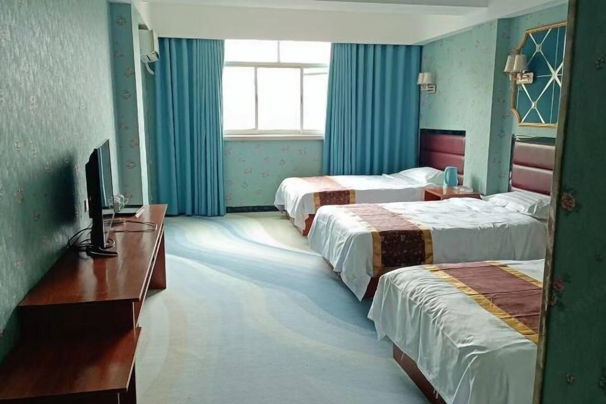 Quarto de hotel com duas camas, uma escrivaninha, televisão e janela com cortinas.