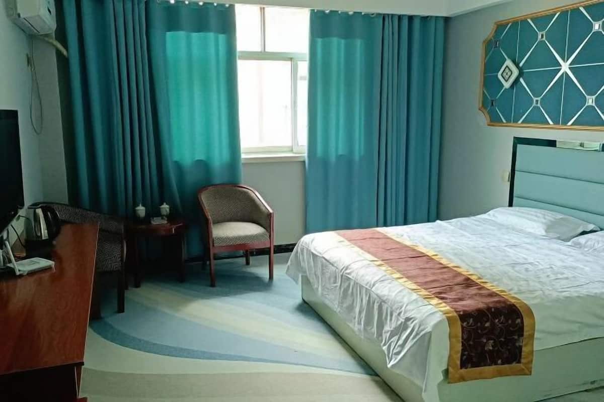 Quarto de hotel com cama, escrivaninha, cadeira e janela com cortinas.