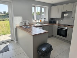 Cozinha moderna com armários cinzas, bancada de madeira, forno embutido e janela com vista para um jardim.