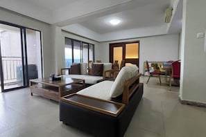 Uma sala de estar moderna com um sofá, mesa de centro e cadeiras. Há uma porta de vidro deslizante que dá para uma varanda.