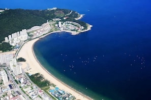 Vista aérea de uma área costeira com uma praia curva, edifícios e uma estrada.