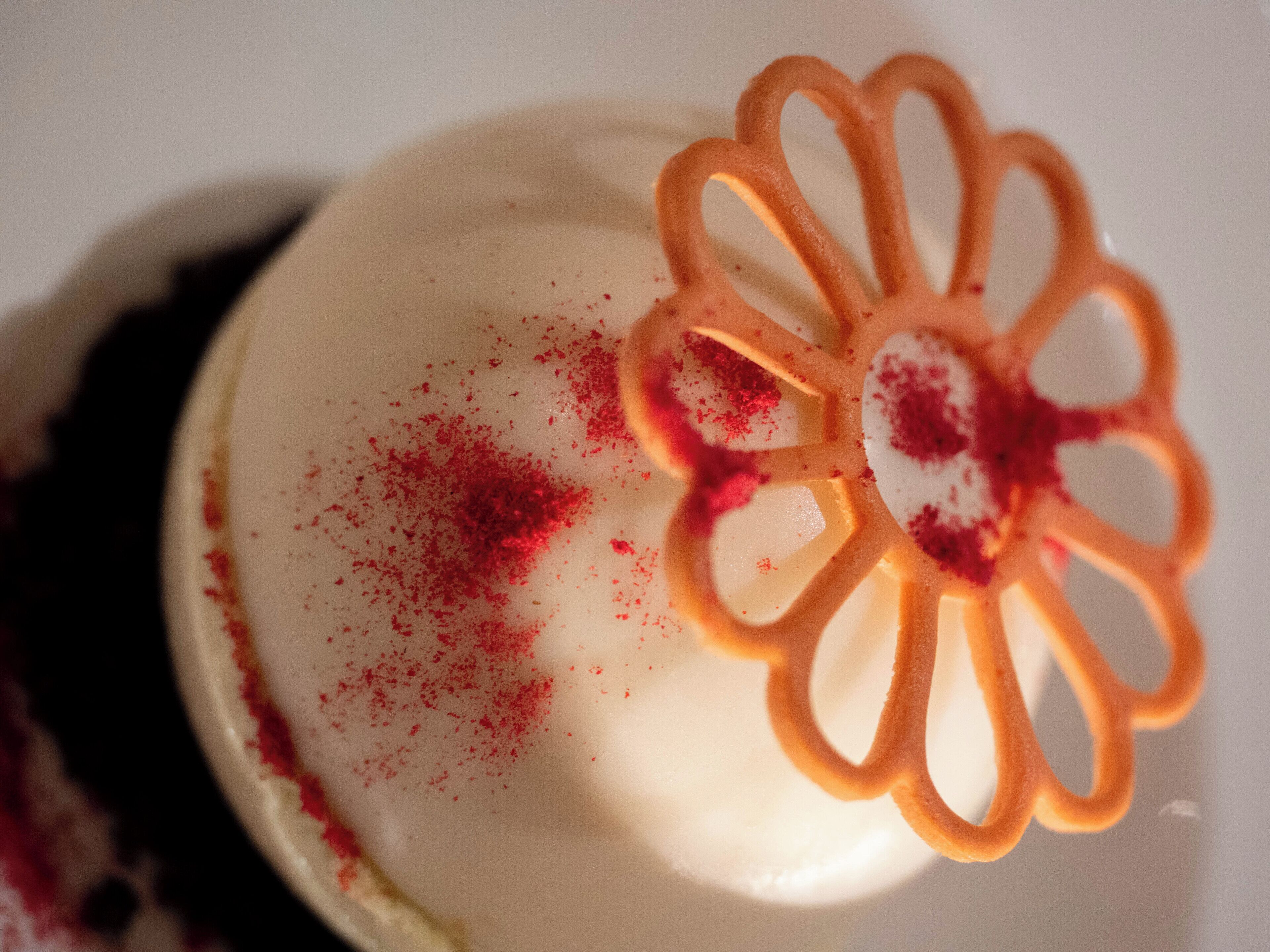 Uma sobremesa com base branca e uma flor laranja decorativa no topo, polvilhada com pó vermelho.