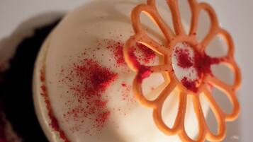 Uma sobremesa com base branca e uma flor laranja decorativa no topo, polvilhada com pó vermelho.