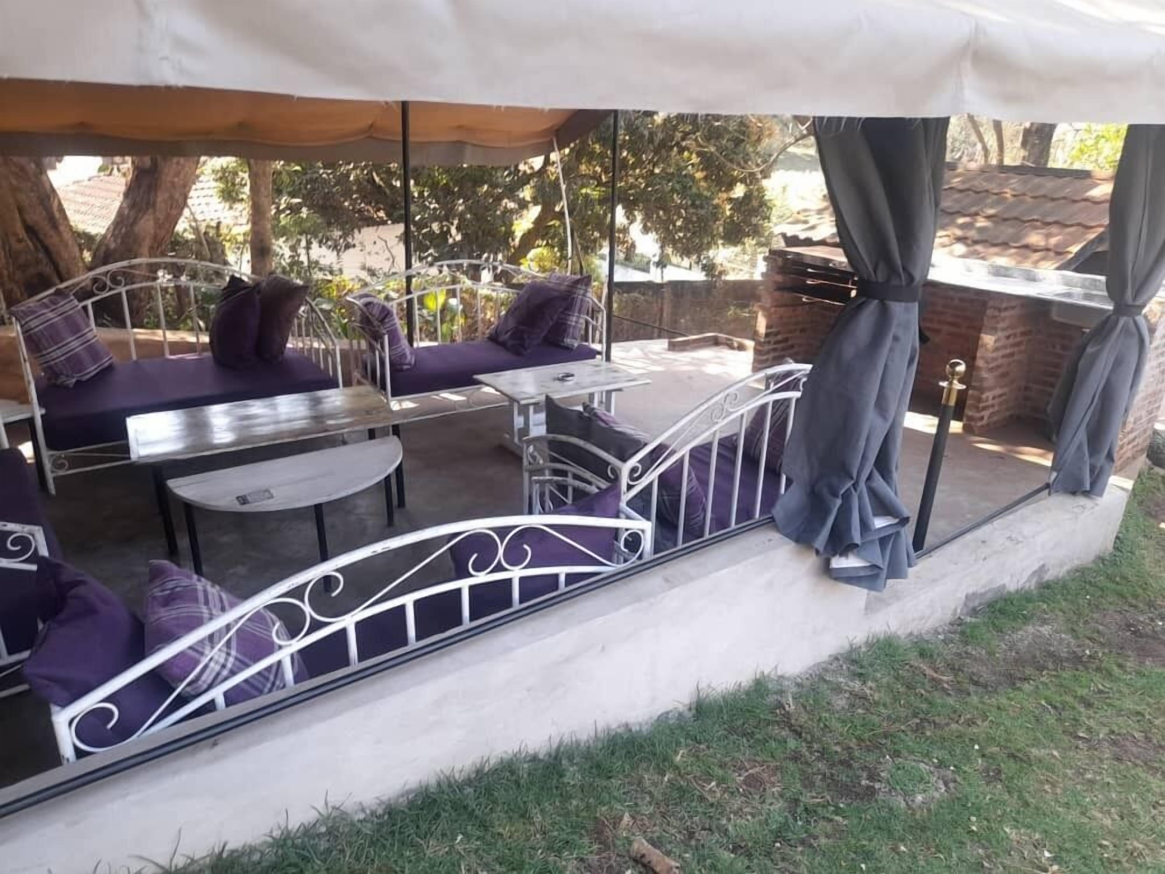 Um pátio externo com assentos e mesas, cercado por uma grade de metal branco e coberto por um toldo.
