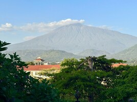 Uma montanha com um edifício de telhado vermelho em primeiro plano, cercada por vegetação.