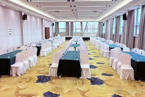 Sala de conferências com mesas compridas, cadeiras brancas e um tapete floral amarelo.