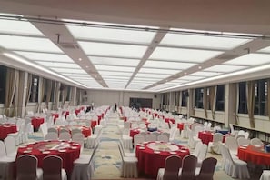 Salão de banquetes com fileiras de mesas, cadeiras e teto alto com claraboias.