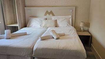 Uma cama de casal com roupa de cama e toalhas brancas, uma cabeceira de madeira com design geométrico e uma mesa de cabeceira com um abajur.