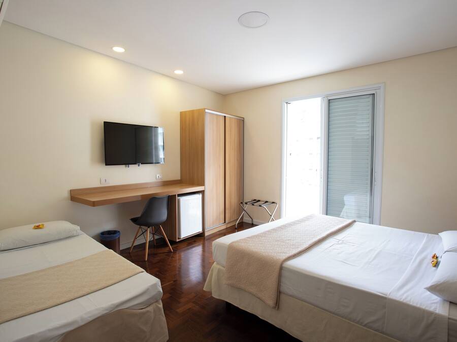 Quarto de hotel com duas camas, uma escrivaninha com cadeira, televisão e guarda-roupa.